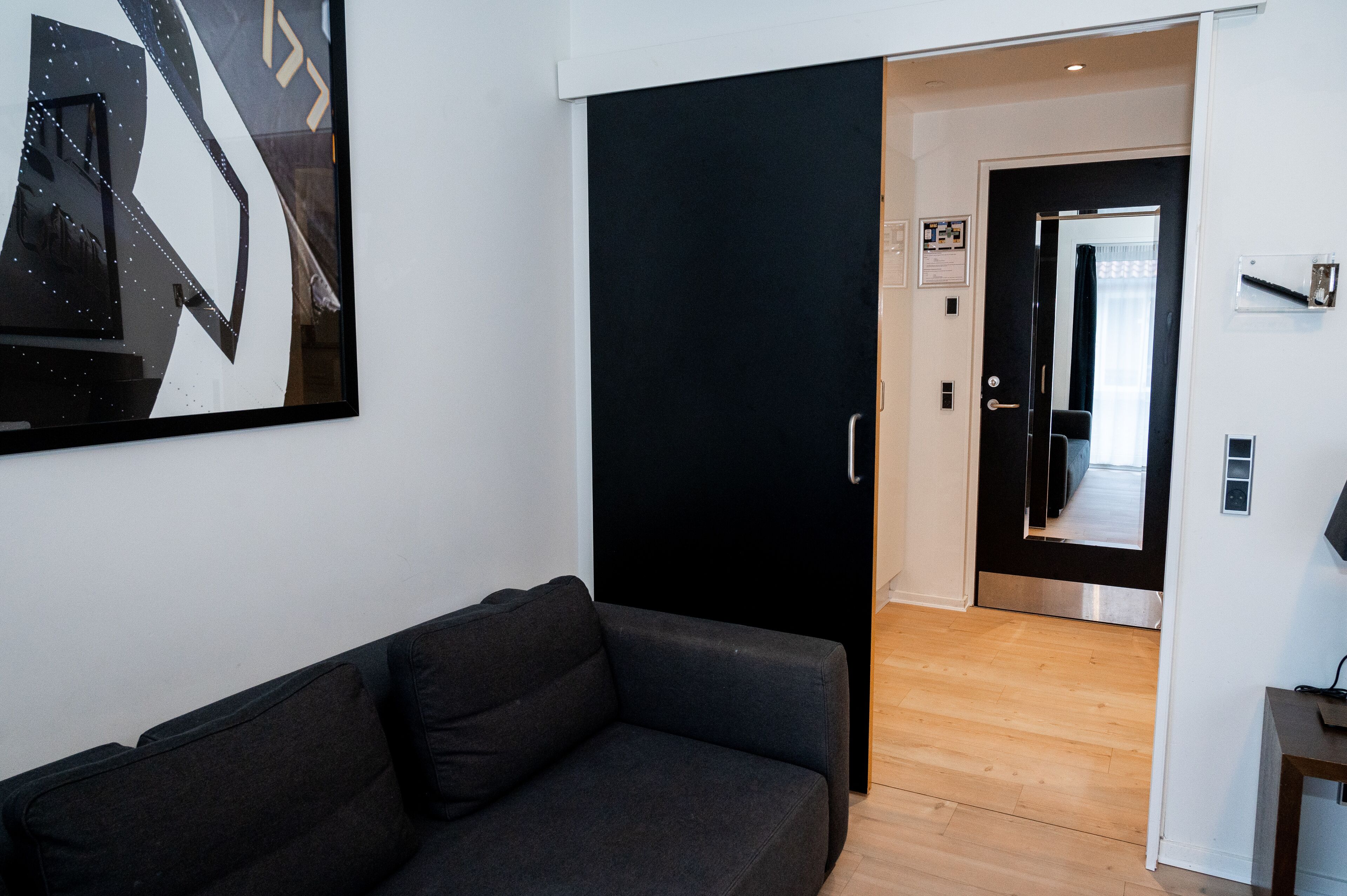 Quarto de hotel moderno com um sofá escuro, uma grande pintura abstrata e piso de madeira.