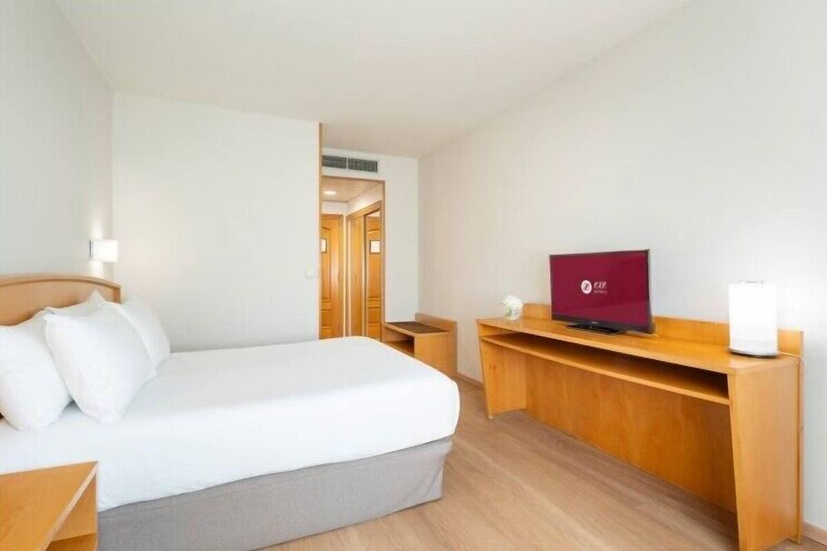 Quarto de hotel com cama, televisão, escrivaninha e abajur.
