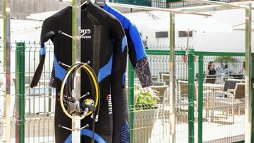 Um fato de neoprene numa estante, com um manómetro e uma mangueira, com o cenário de uma área externa cercada, com mesas e cadeiras.