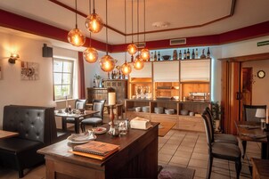 Interior de restaurante com área de bar, mesas e cadeiras, e cozinha ao fundo.