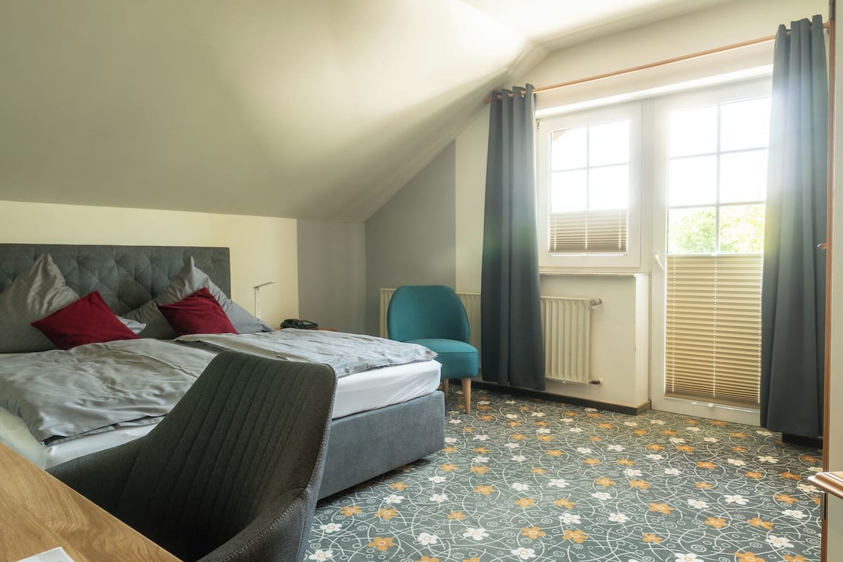 Quarto com uma cama, uma cadeira, um radiador e uma janela com cortinas.