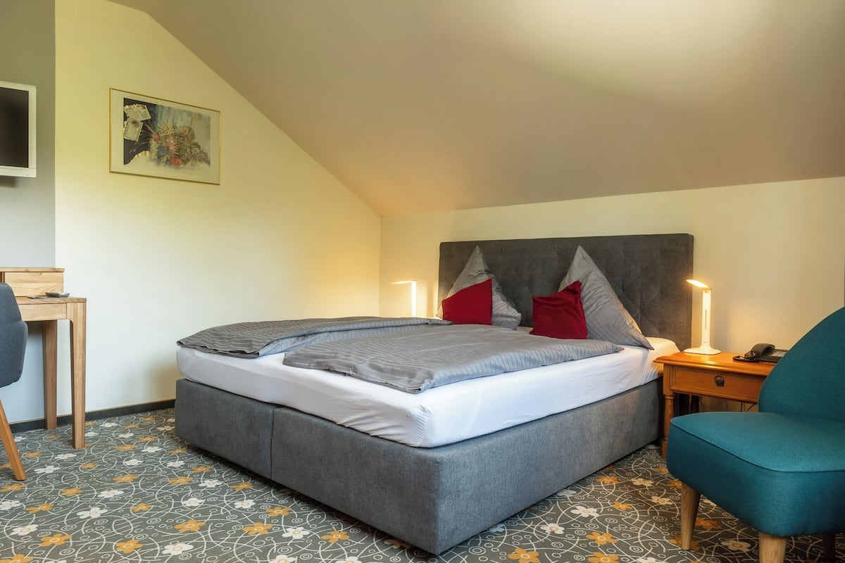 Quarto com cama, luminárias de cabeceira, escrivaninha e uma cadeira.