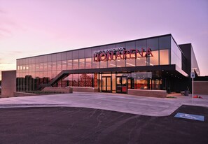 Um edifício moderno com fachada de vidro ampla, entrada destacada e uma placa com a inscrição 'SEARCY HIGH SCHOOL LIONARENA'.