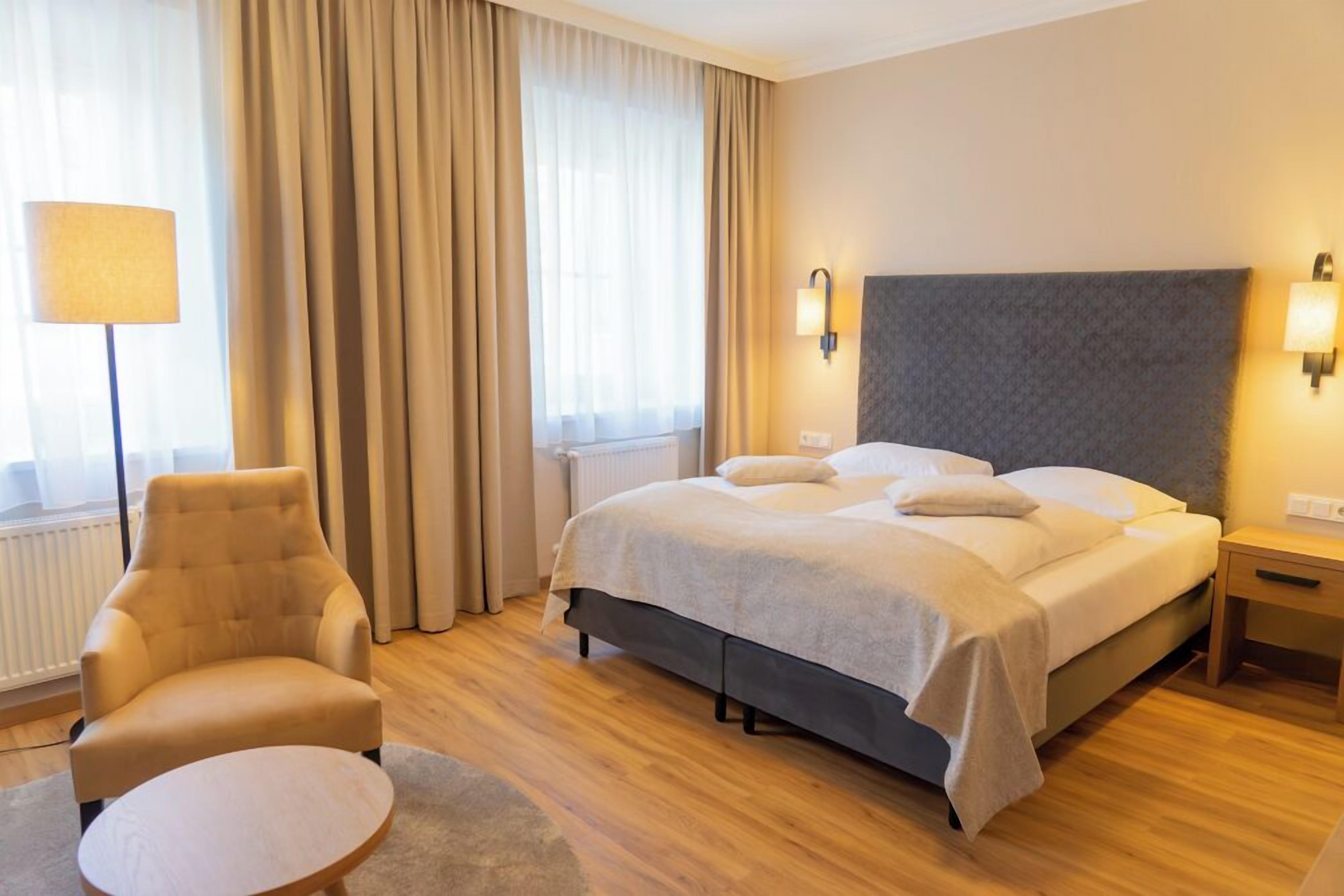 Quarto de hotel com cama, cadeira, mesa de cabeceira e abajur.
