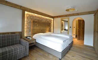 Quarto moderno com parede de detalhes em pedra, cabeceira de madeira, cama grande, mesa de cabeceira com telefone e sofá xadrez.