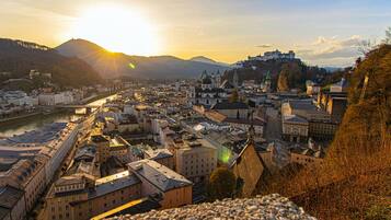 Paisagem urbana histórica com um castelo imponente numa colina, um rio serpenteando pelo centro e uma mistura de edifícios tradicionais e modernos.