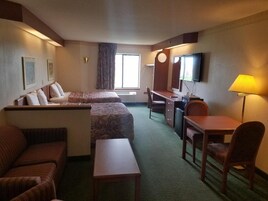 Quarto de hotel com cama, escrivaninha, cadeira, sofá e televisão.