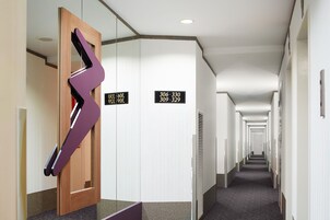 Corredor de hotel com design moderno, incluindo uma porta roxa única e placas de sinalização.