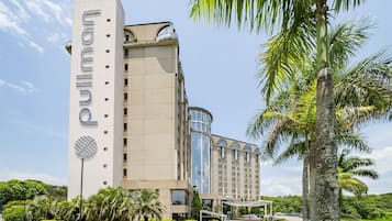 Um hotel com um grande letreiro 'Pullman', design arquitetônico moderno e área externa bem cuidada, com palmeiras e uma galeria coberta.
