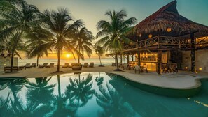 Resort com piscina, espreguiçadeiras e área de bar coberta por um telhado de palha.