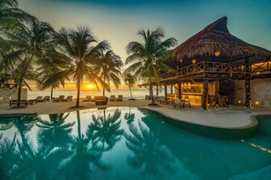 Piscina de resort com palmeiras, espreguiçadeiras e uma estrutura de telhado de palha.