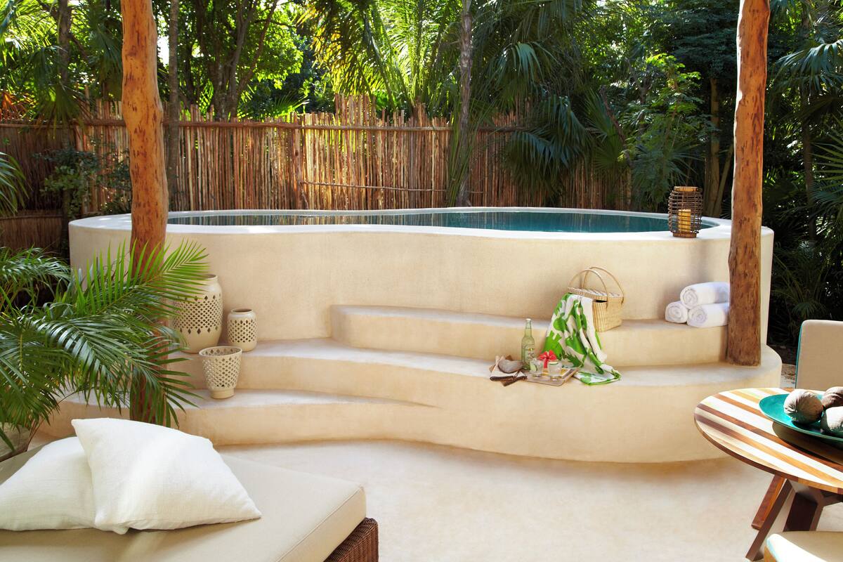 Área de piscina com escadas que levam a uma banheira de hidromassagem, cercada por vegetação exuberante e cercas de bambu.