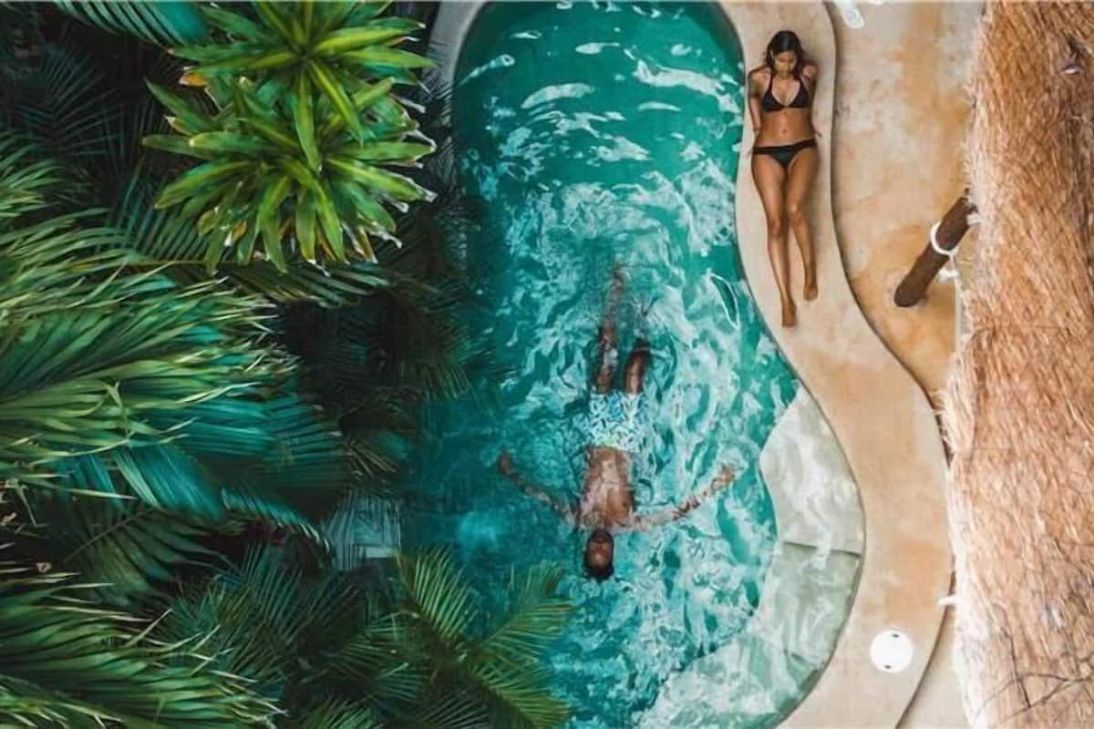 Piscina com duas pessoas nadando, rodeada por vegetação exuberante.