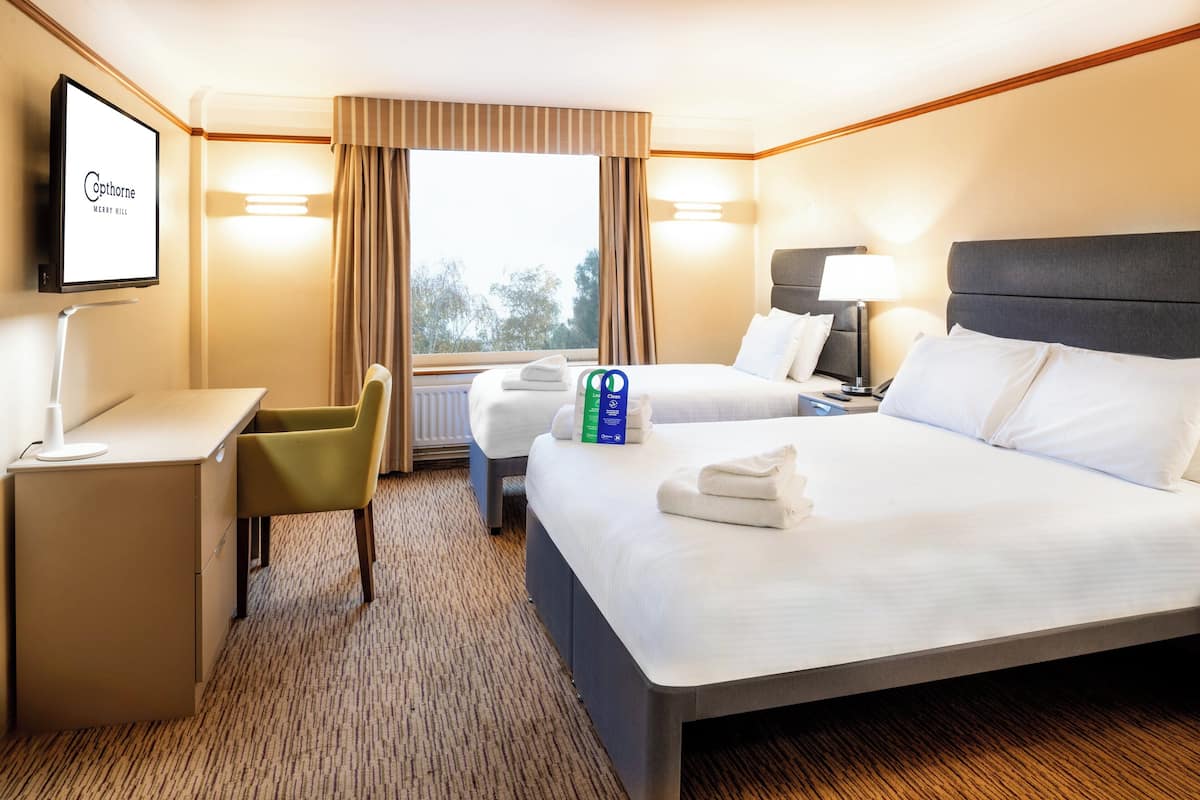 Quarto de hotel com cama grande, escrivaninha, cadeira e televisão na parede.