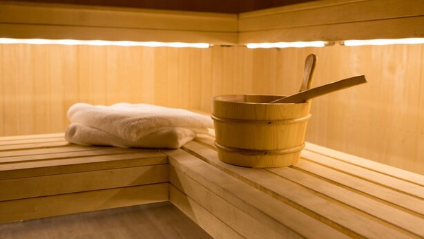 Uma sauna de madeira com um banco, um balde e uma toalha.
