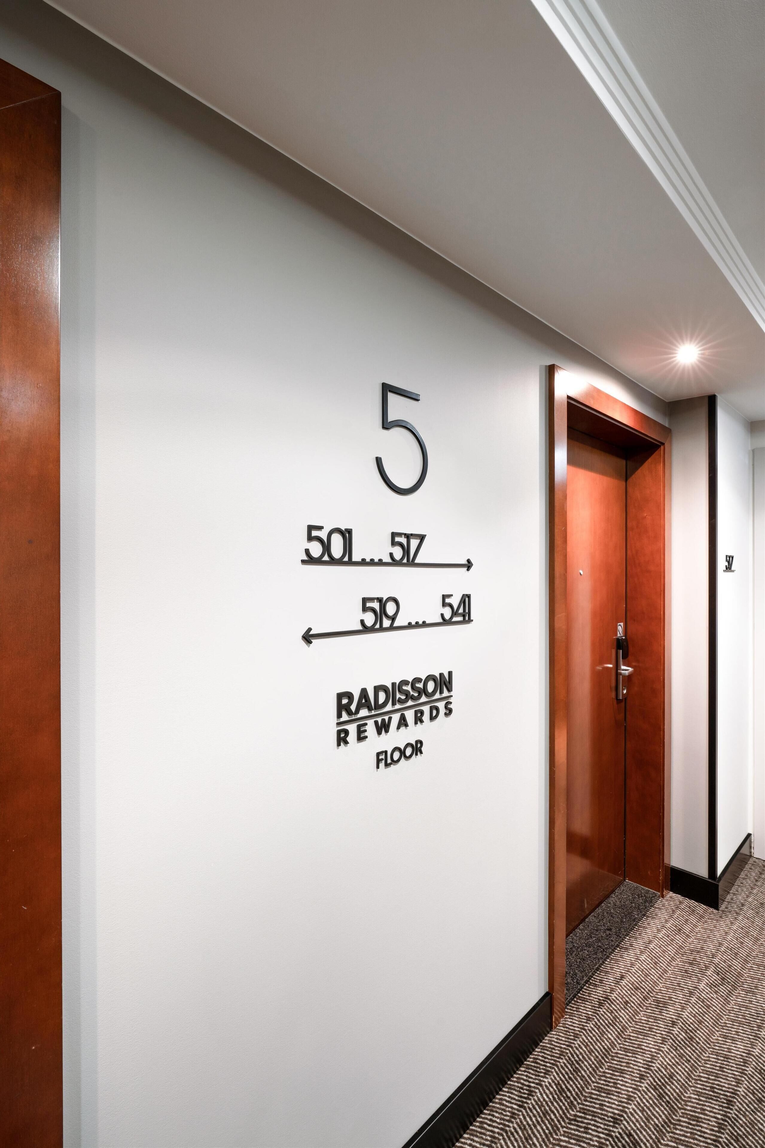 Corredor com placa na parede indicando o andar Radisson Rewards, com setas direcionais para os quartos 501 a 507 e 519 a 541.