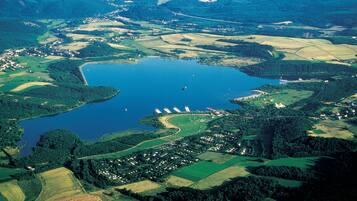Vista aérea de um lago rodeado por campos verdes e uma pequena aldeia com casas e caminhos.