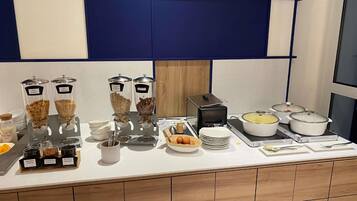 Disposição de buffet com diversos distribuidores de alimentos, pratos e pratos quentes.