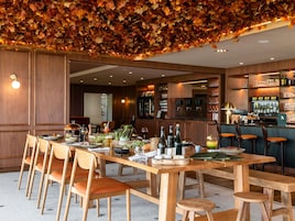Um restaurante com uma longa mesa de madeira, cadeiras e um espaço de bar com prateleiras cheias de garrafas e copos.