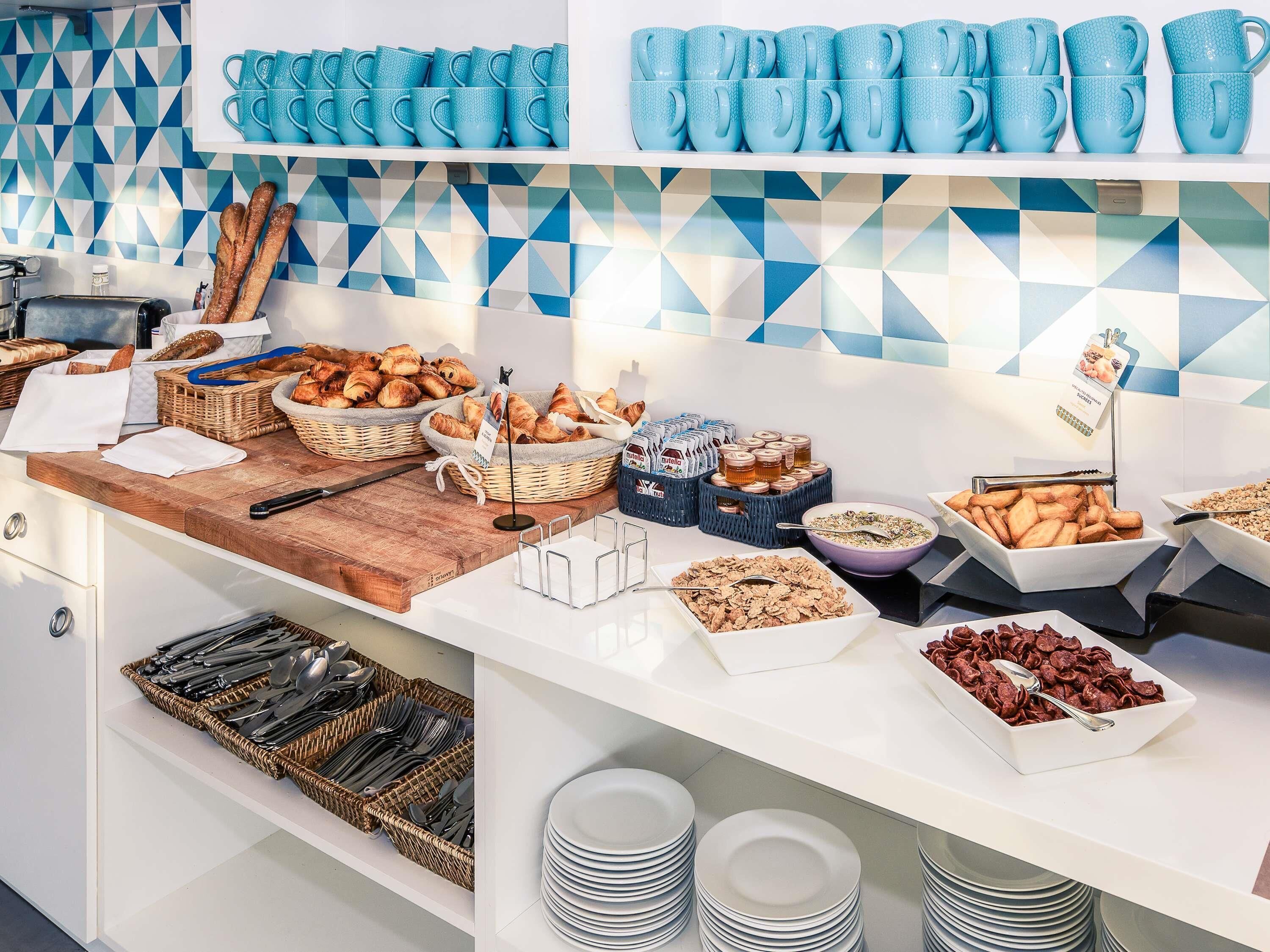 Disposição de buffet com diversos alimentos, utensílios e copos azuis em prateleiras.