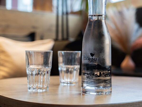 Uma garrafa de água Eau de Genève, dois copos e uma mesa de madeira.