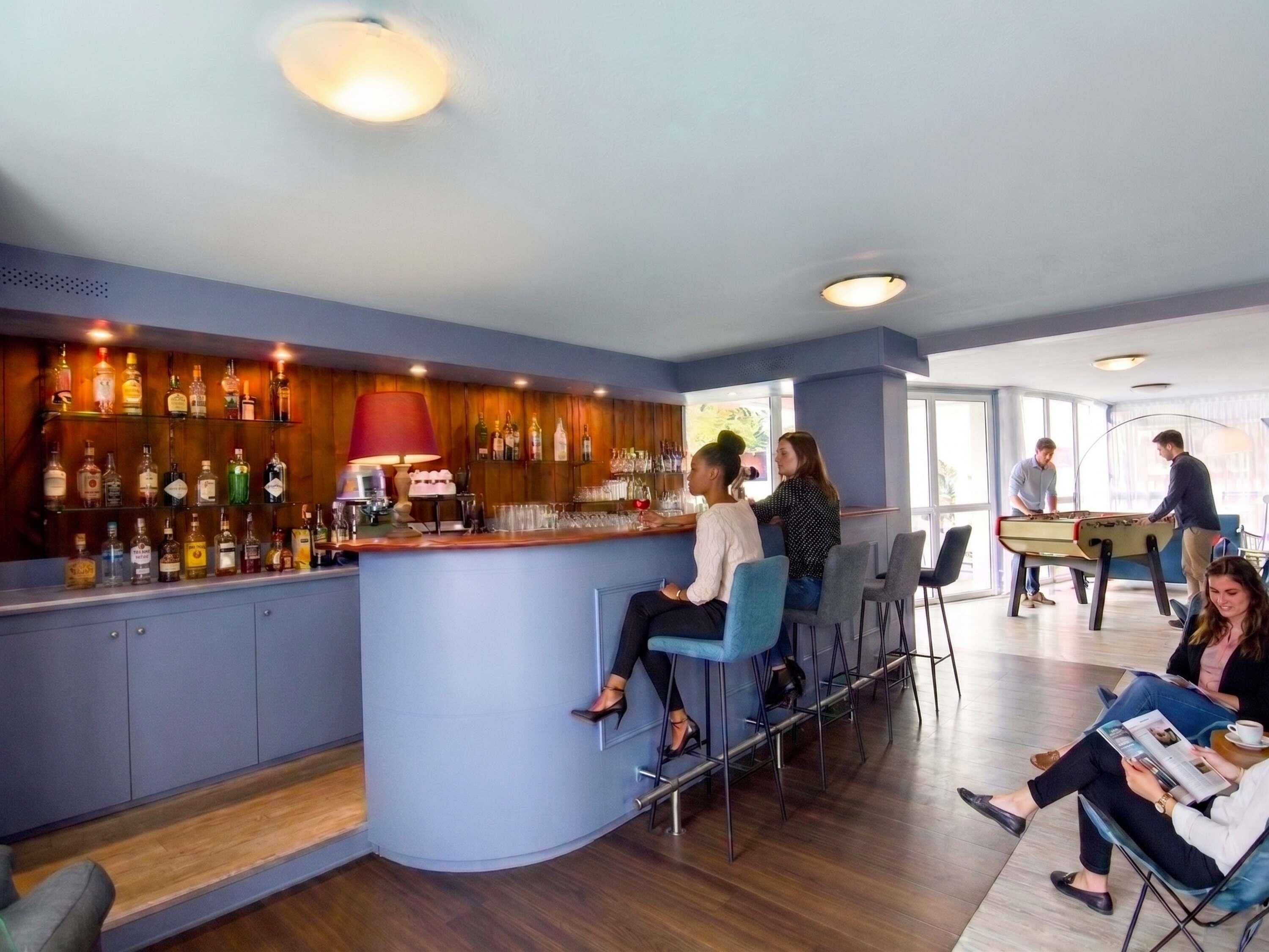 Uma área de bar com balcão, banquetas e mesa de bilhar em um interior moderno.