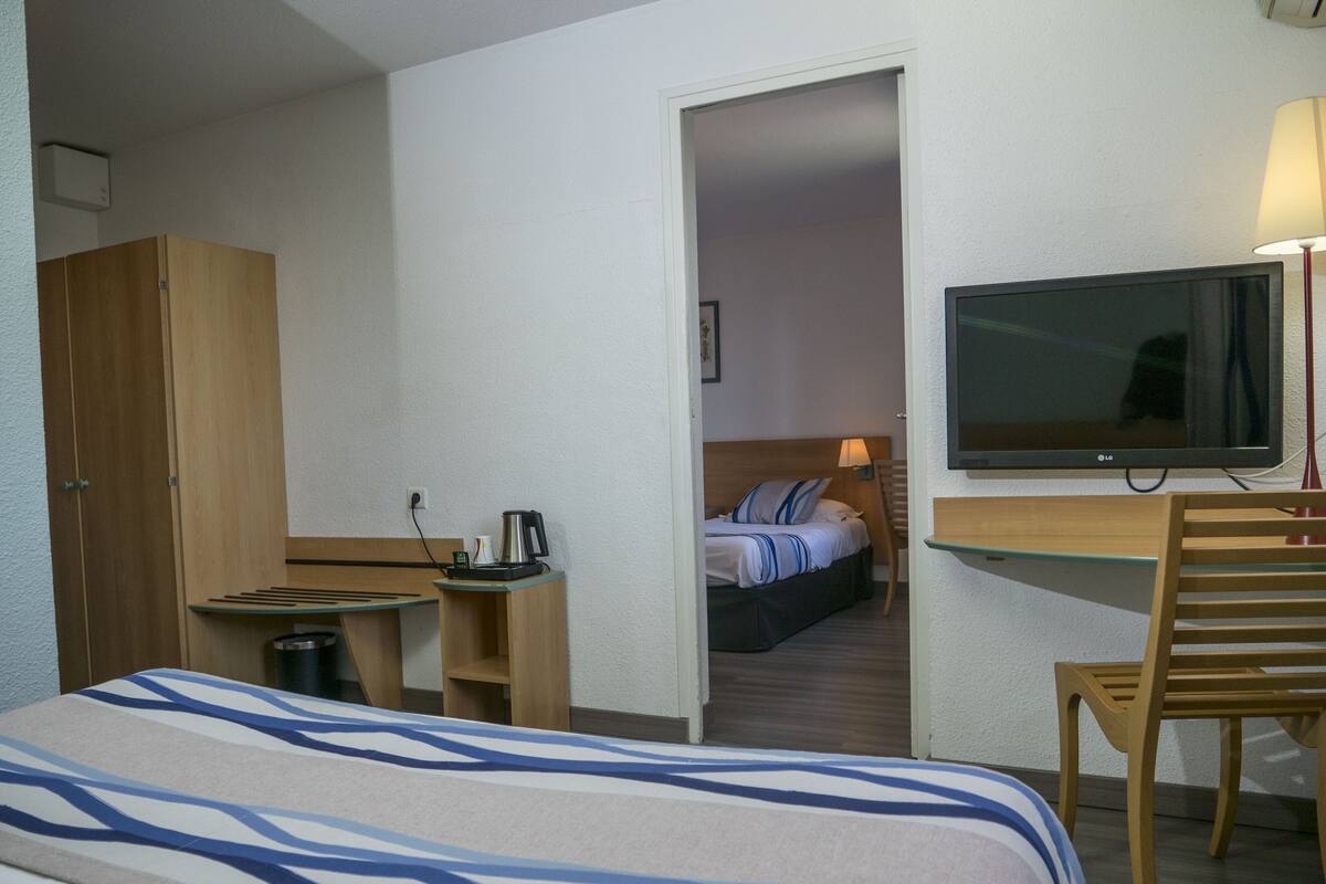Quarto de hotel com cama, escrivaninha, televisão e guarda-roupa.