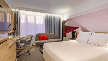 Quarto de hotel moderno com uma cama grande, um sofá, uma escrivaninha e uma televisão.