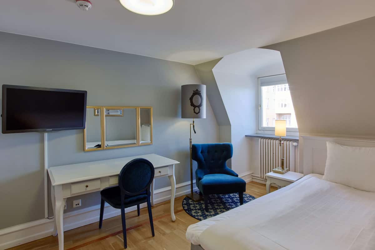 Quarto com cama, escrivaninha, cadeira, televisão, abajur e janela.