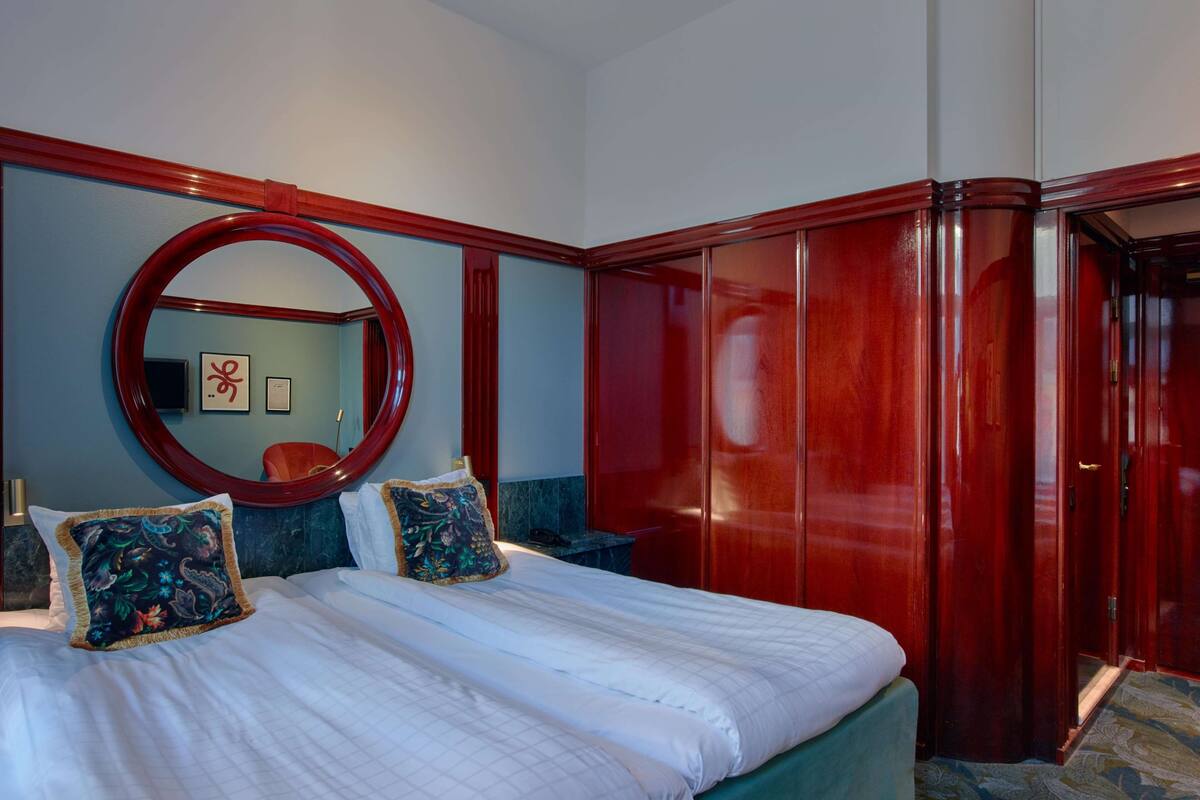 Quarto de hotel com uma cama grande, um espelho redondo e um guarda-roupa.