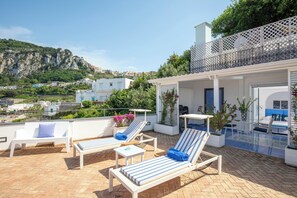 Um terraço no telhado com duas espreguiçadeiras, uma mesa pequena e um espaço de estar com vista para a paisagem ao redor.