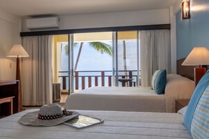 Quarto de hotel com duas camas, varanda com vista para palmeiras e ar condicionado no teto.