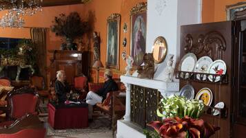 Uma sala de estar ampla com lareira, poltronas estofadas em vermelho e um candelabro.