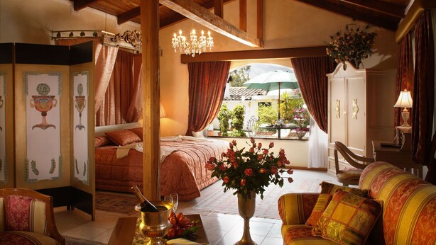 Quarto com cama, sofá, lustre e vista para o exterior.