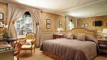 Quarto bem equipado com uma cama grande, um espaço de estar com uma poltrona, uma escrivaninha e um espelho grande.