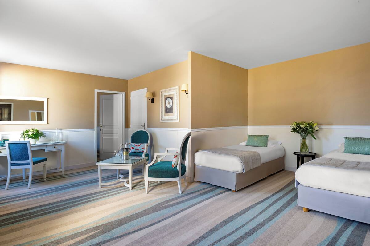 Quarto de hotel com cama, duas cadeiras, escrivaninha e uma mesinha.