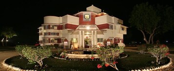 Um edifício de vários andares com um pátio central, rodeado por um jardim bem cuidado com diversas plantas e uma pequena fonte.