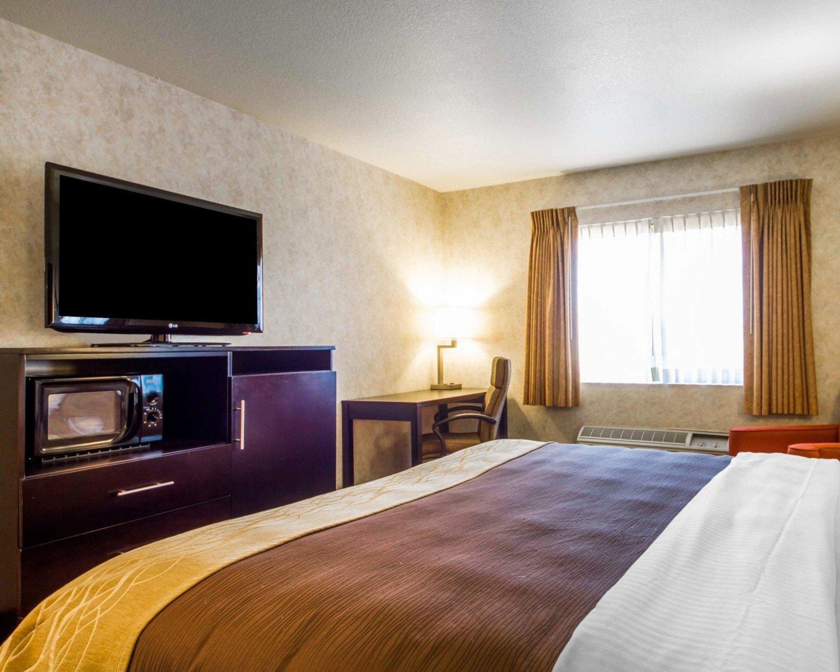 Quarto de hotel com cama, televisão, micro-ondas, escrivaninha e janela com cortinas.