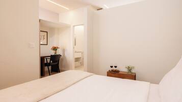 Quarto de hotel moderno com uma cama, uma escrivaninha e uma mesa de cabeceira com duas taças de vinho.