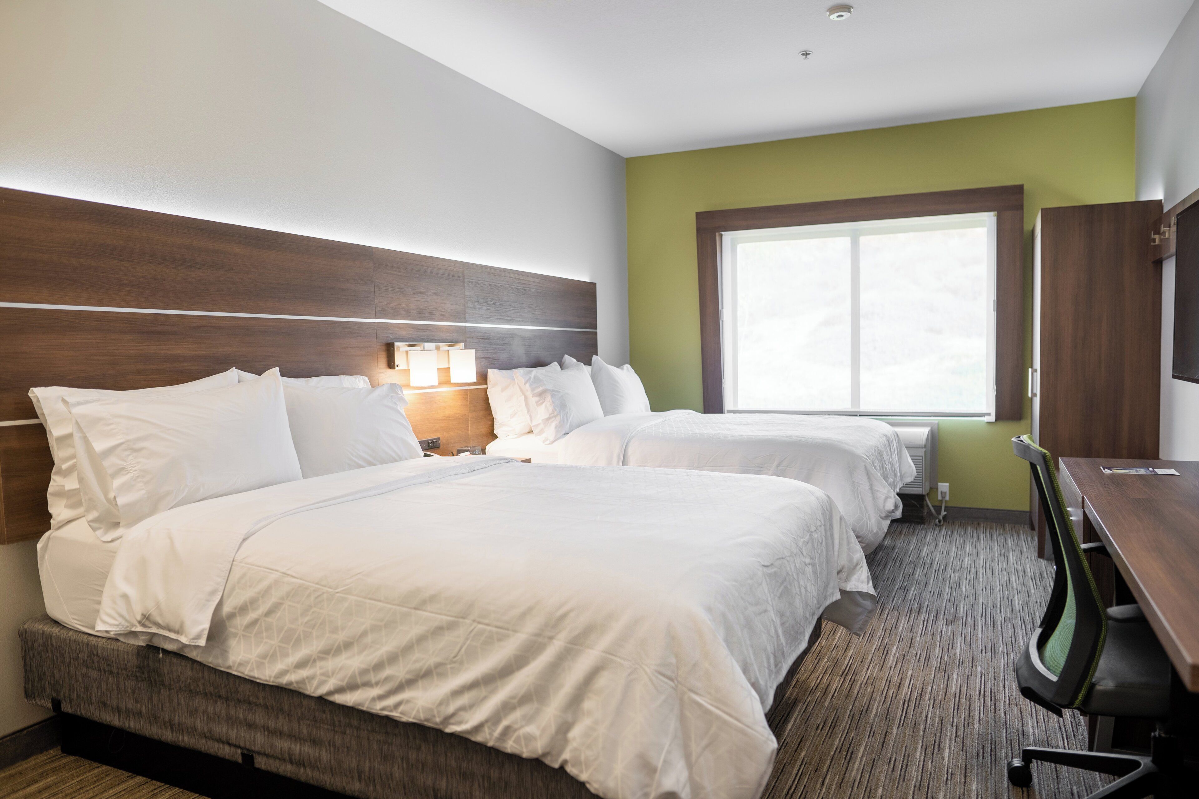 Quarto de hotel com duas camas, uma escrivaninha e uma janela.