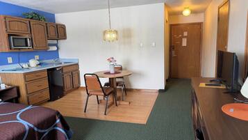 Quarto de hotel compacto com cozinha compacta, área de jantar com mesa e cadeiras, cama e televisão.