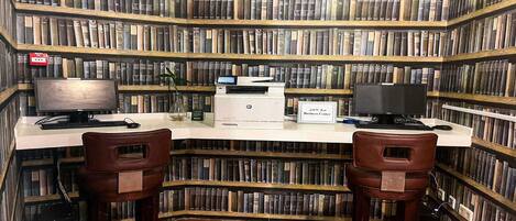 Uma biblioteca com estantes repletas de livros, duas mesas com computadores e duas cadeiras.