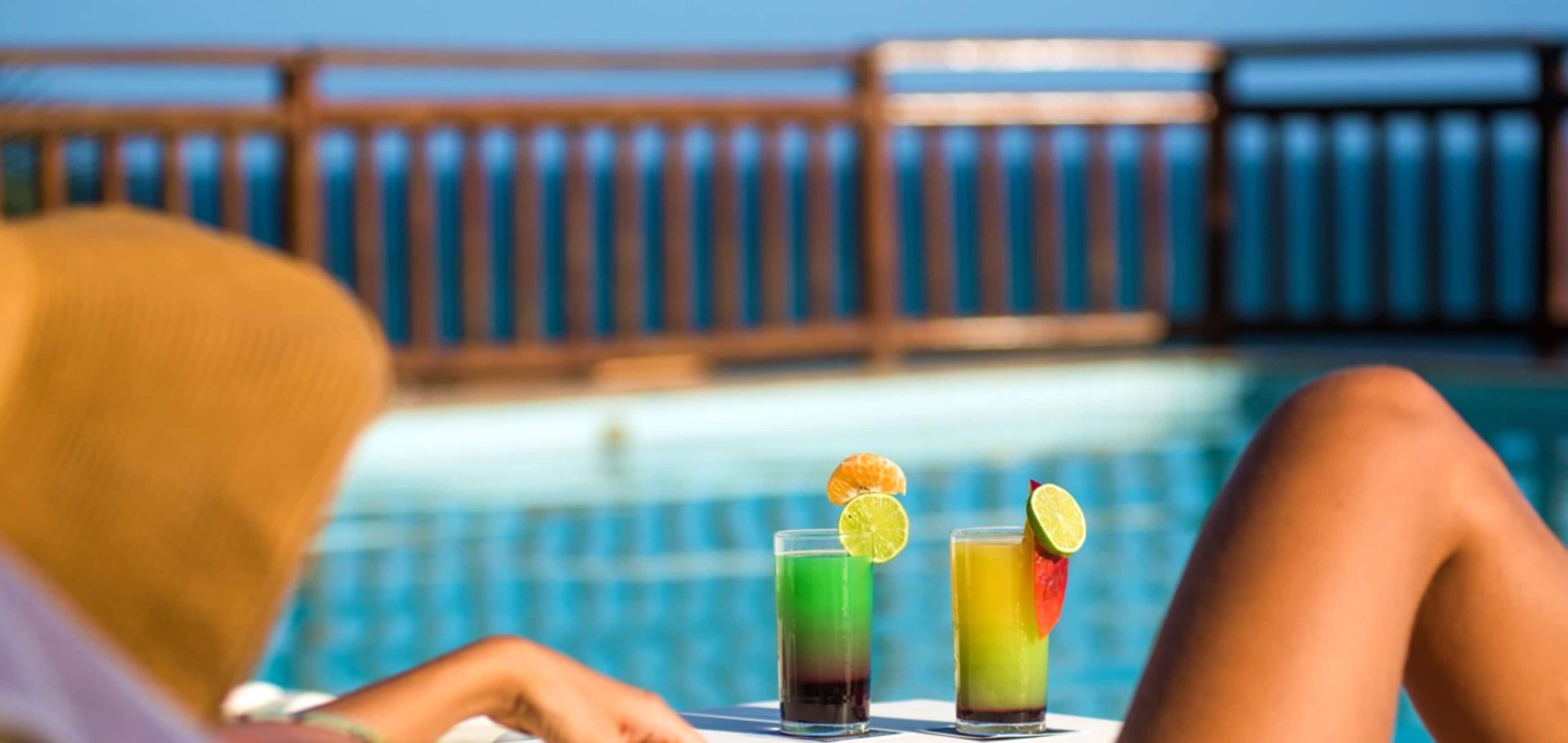 Uma pessoa relaxando perto de uma piscina, com duas bebidas sobre a mesa.