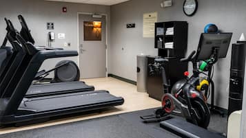 Centro de fitness com esteiras, bicicleta ergométrica e relógio de parede.