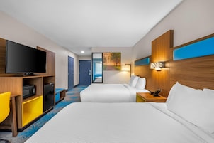 Quarto de hotel com duas camas, uma televisão, uma secretária com computador e um quadro na parede.