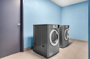 Uma lavanderia com duas máquinas de lavar de abertura frontal, uma porta e paredes azul-claras.