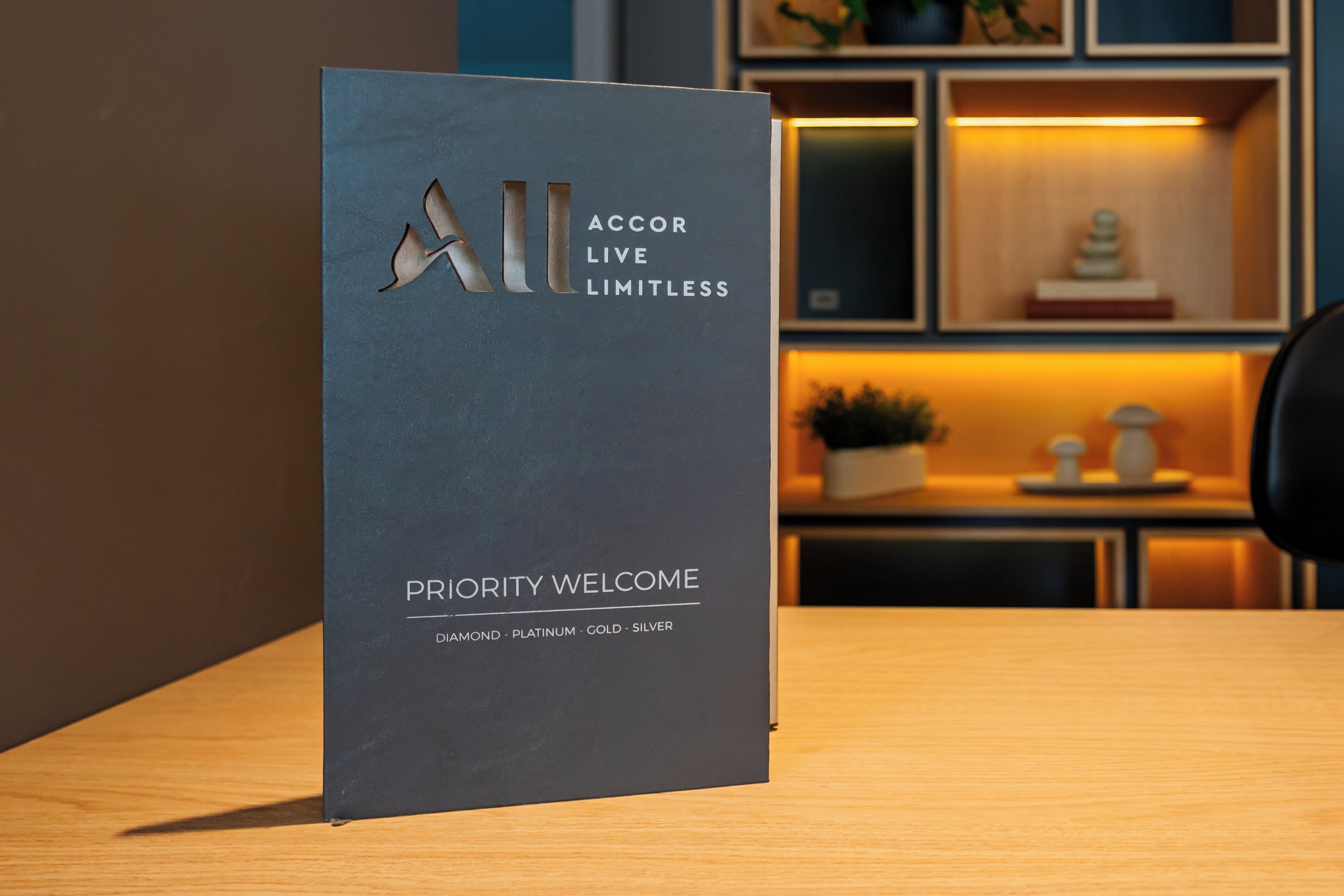 Um balcão de recepção com uma placa indicando "Priority Welcome" e "Accor Live Limitless", oferecendo opções de hospedagem em diamante, platina, ouro e prata.