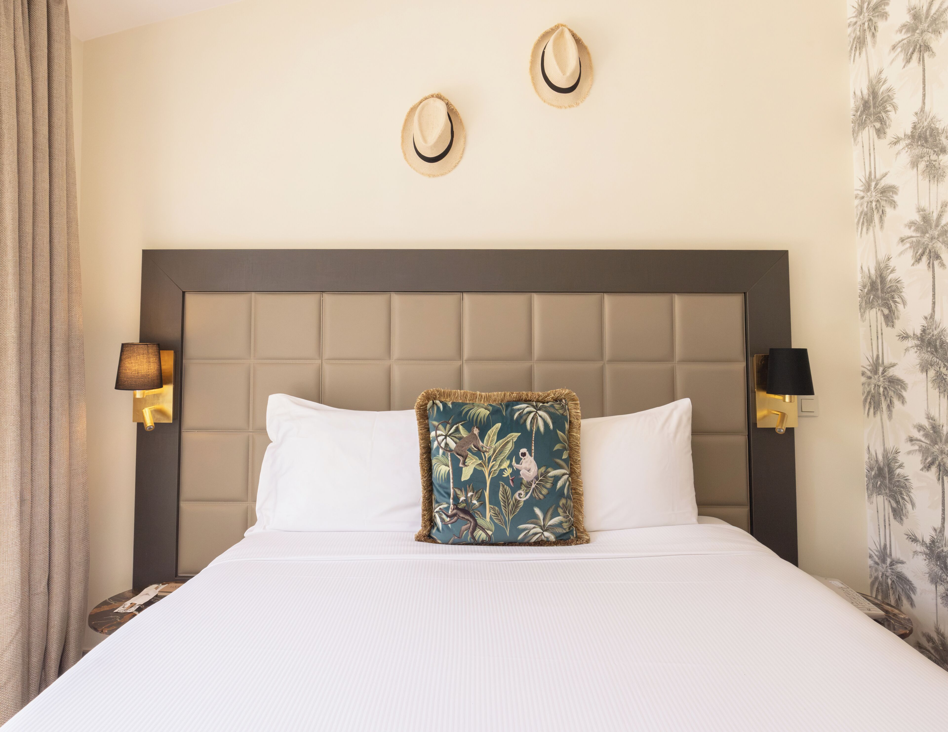 Quarto de hotel com uma cama grande, duas luminárias fixadas na parede e cabeceira com design acolchoado.