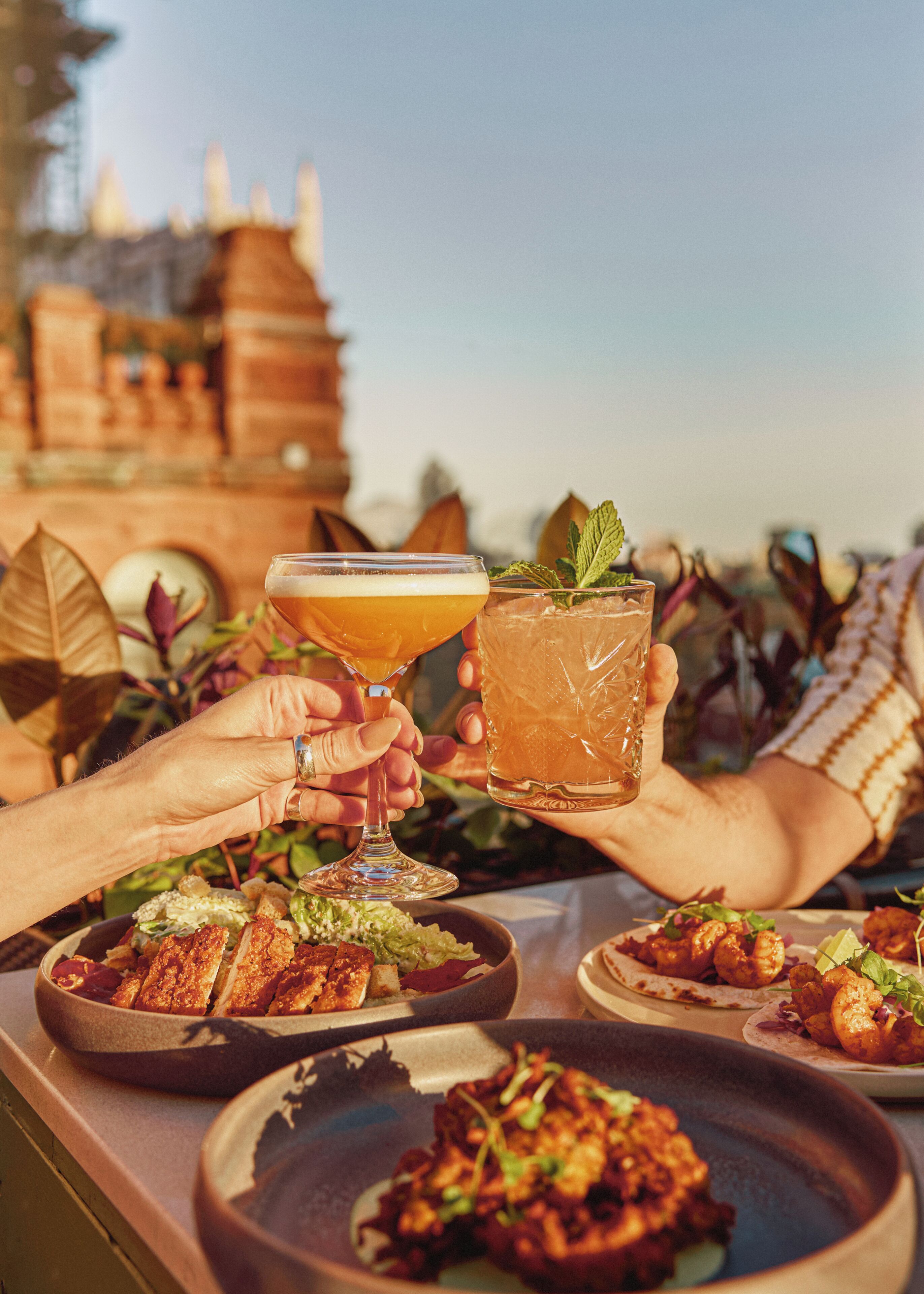 Uma mesa com comida e bebidas, um edifício ao fundo e um céu limpo.
