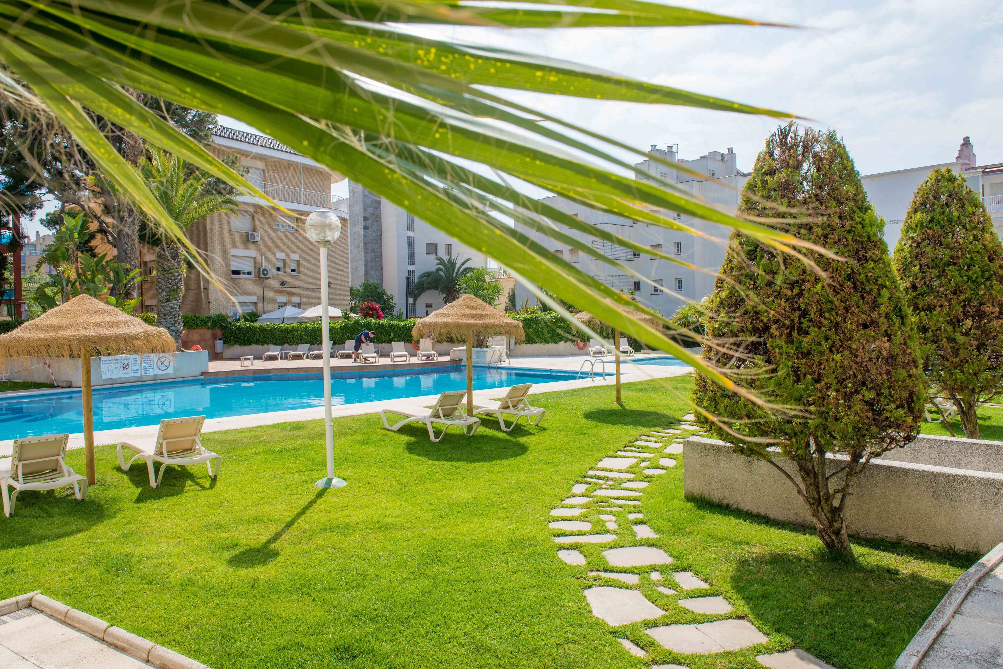 Uma área de piscina com espreguiçadeiras, um caminho de pedra e um gramado bem cuidado.